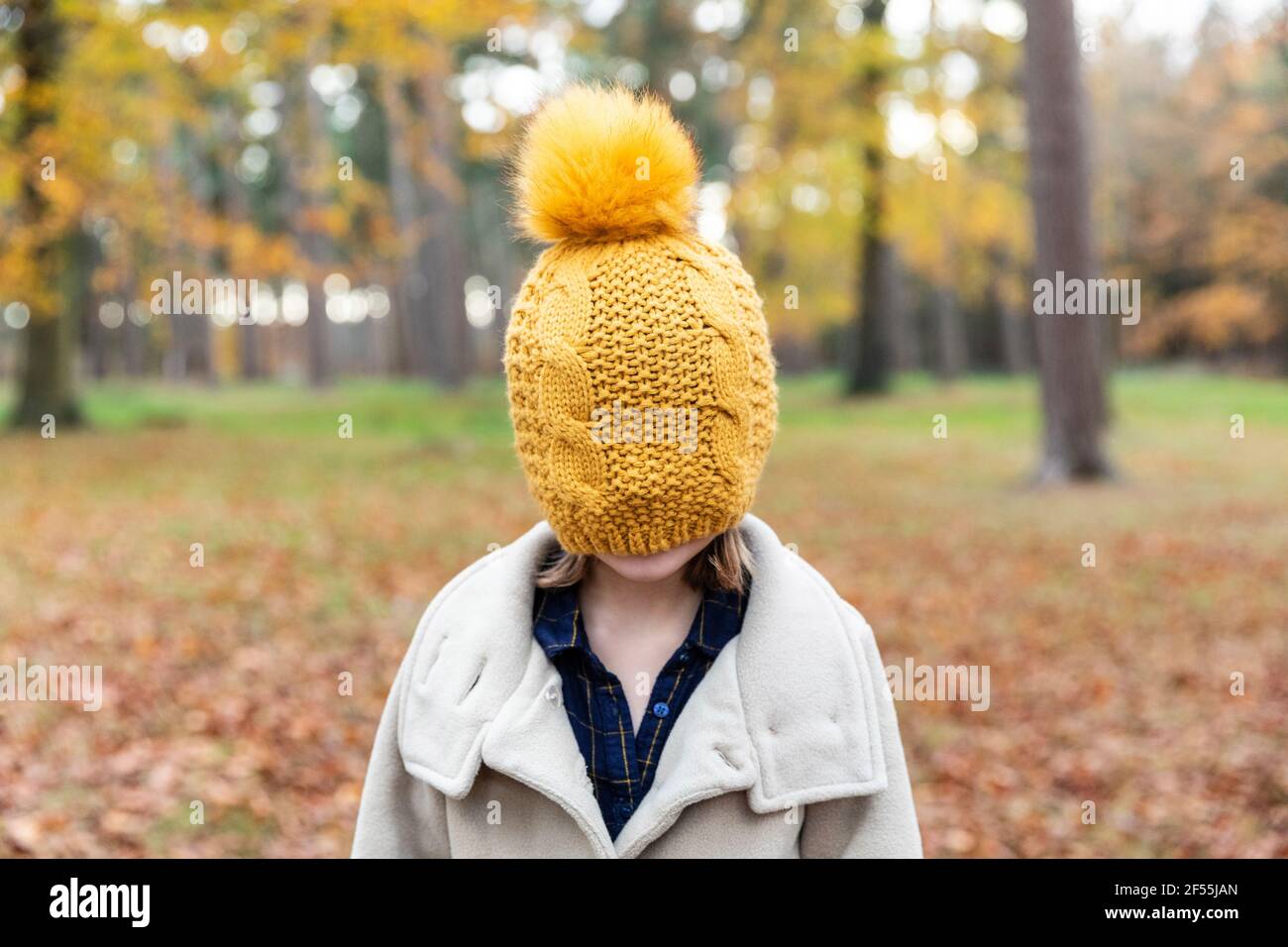 Girl wearing jacket covering face with knit hat while standing at ...