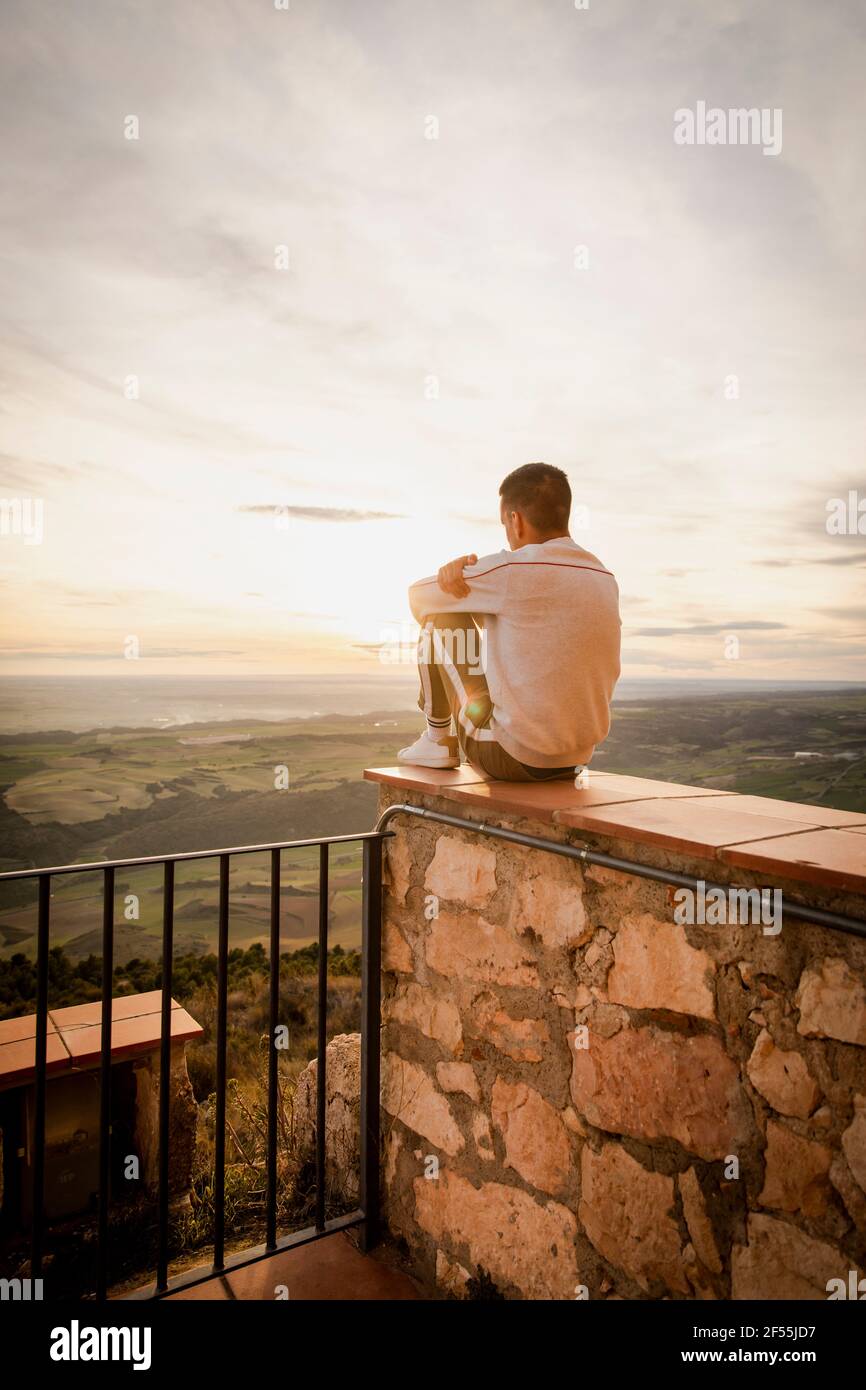Young man sitting on retaining wall during sunset Stock Photo - Alamy