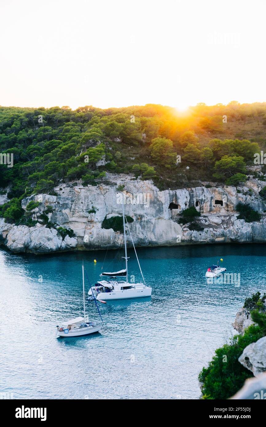 Nautical vessels moored in sea against cliff during sunset Stock Photo ...