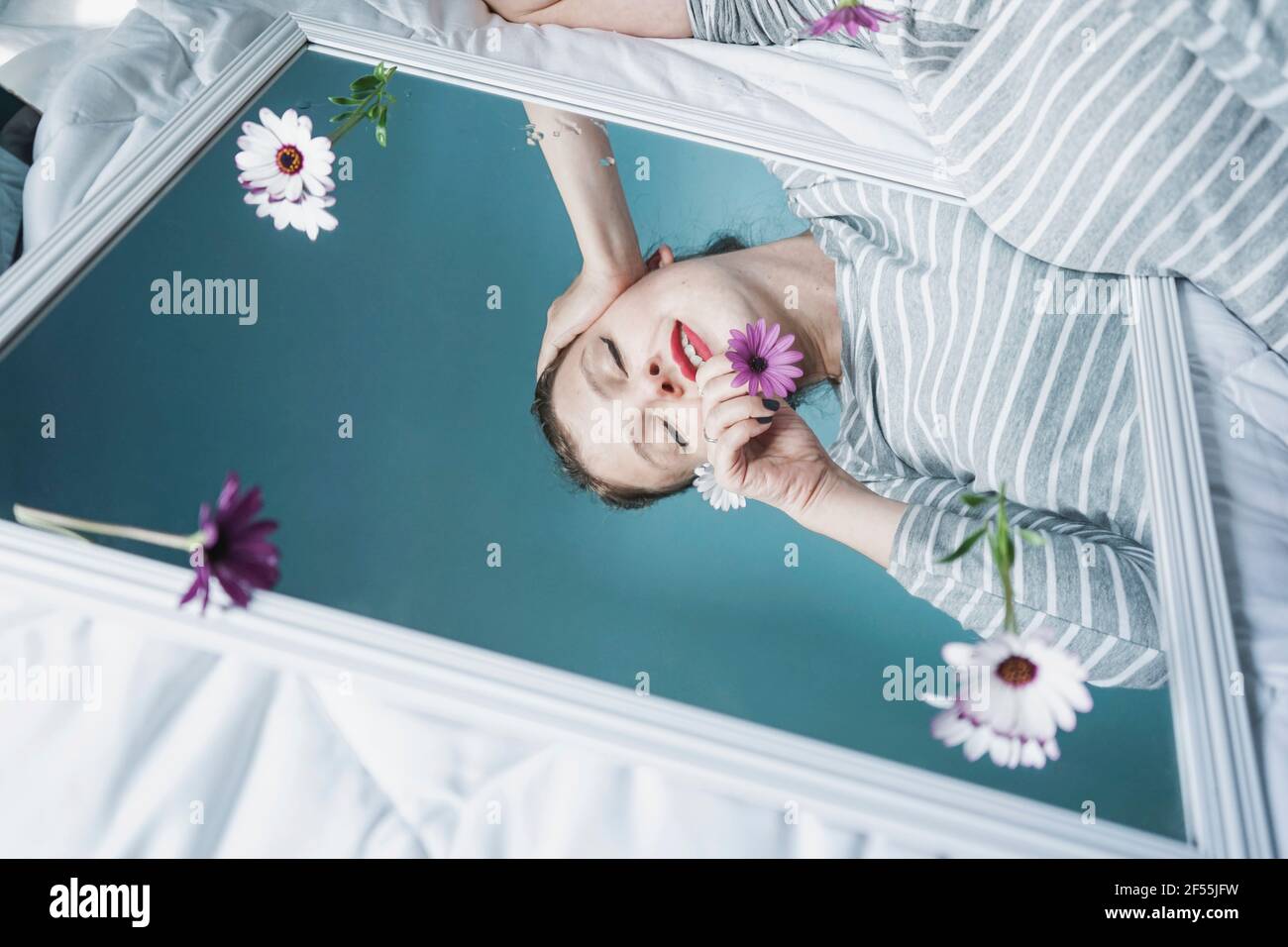 Young woman reflecting in mirror lying on bed Stock Photo - Alamy