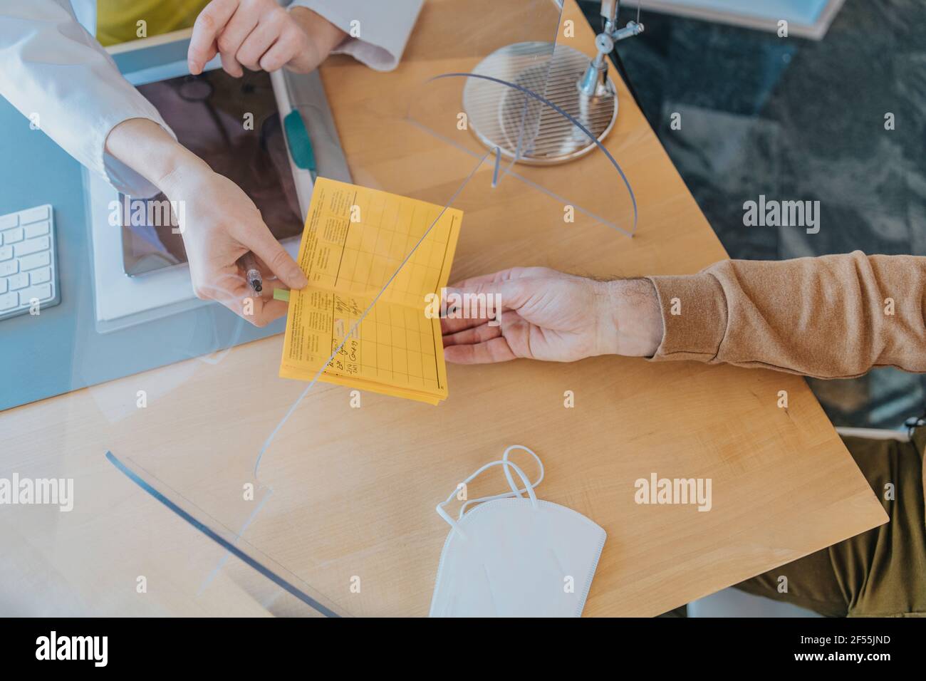 Doctor giving vaccination certificate to patient while sitting behind ...