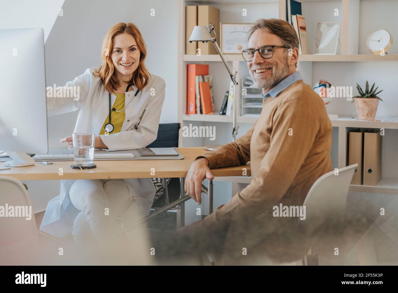 Female doctor and patient smiling while sitting at doctor's office ...