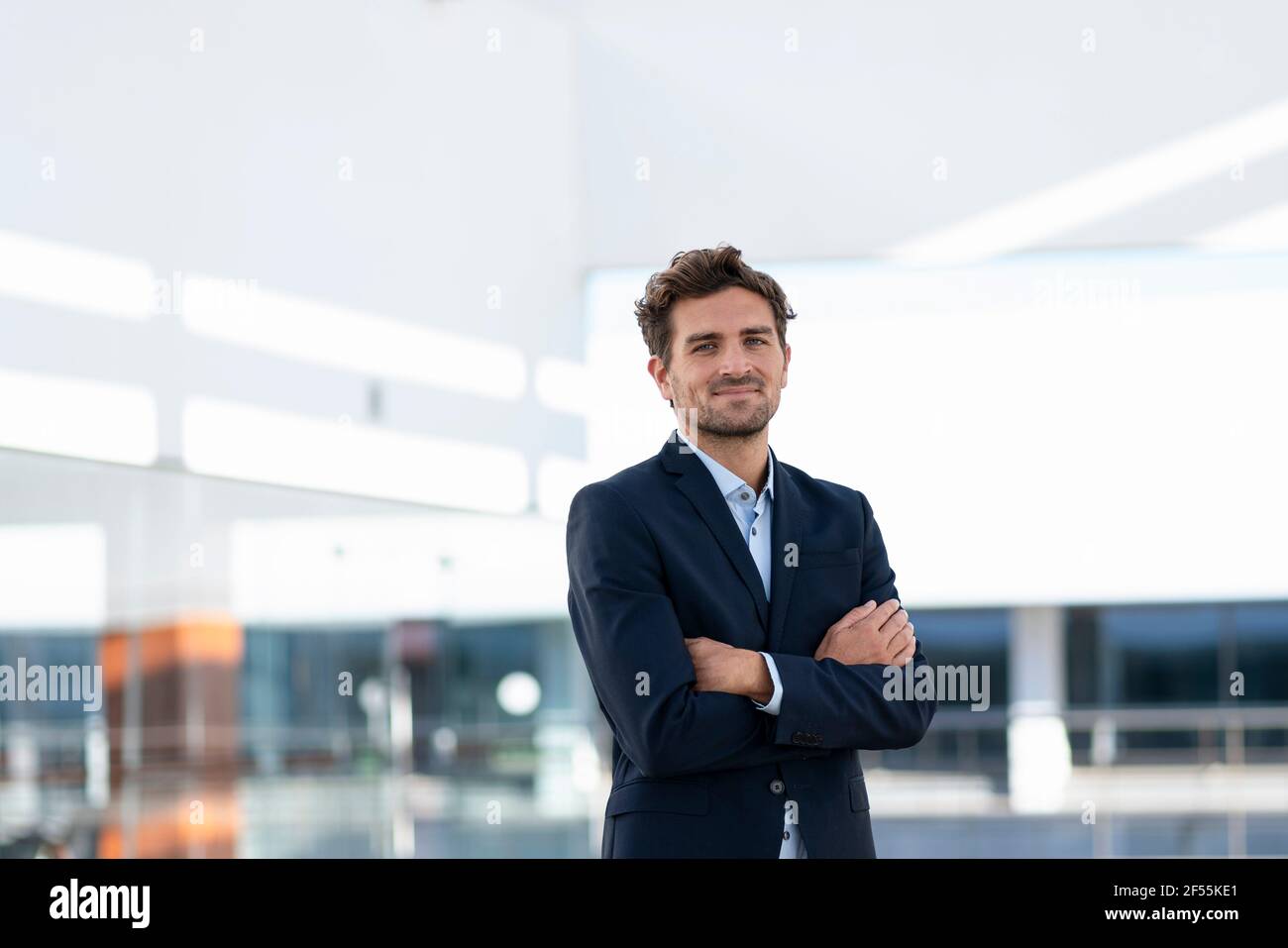 Businessman smiling while standing with arms crossed against office ...
