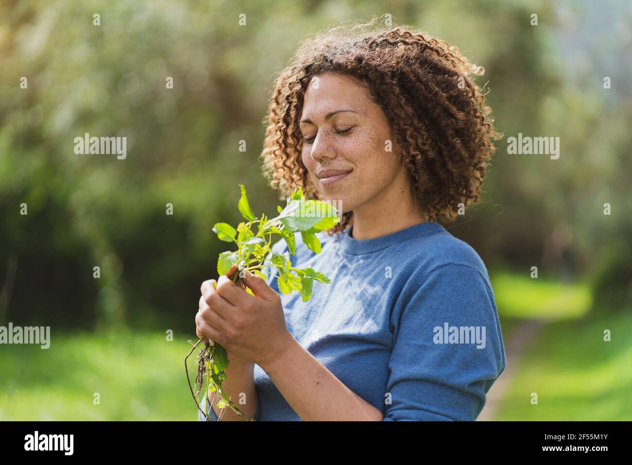 Curly haired woman smelling mint leaves in garden Stock Photo - Alamy