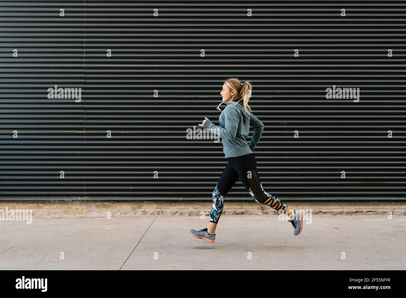 Female athlete running on sidewalk by wall during sports training Stock ...