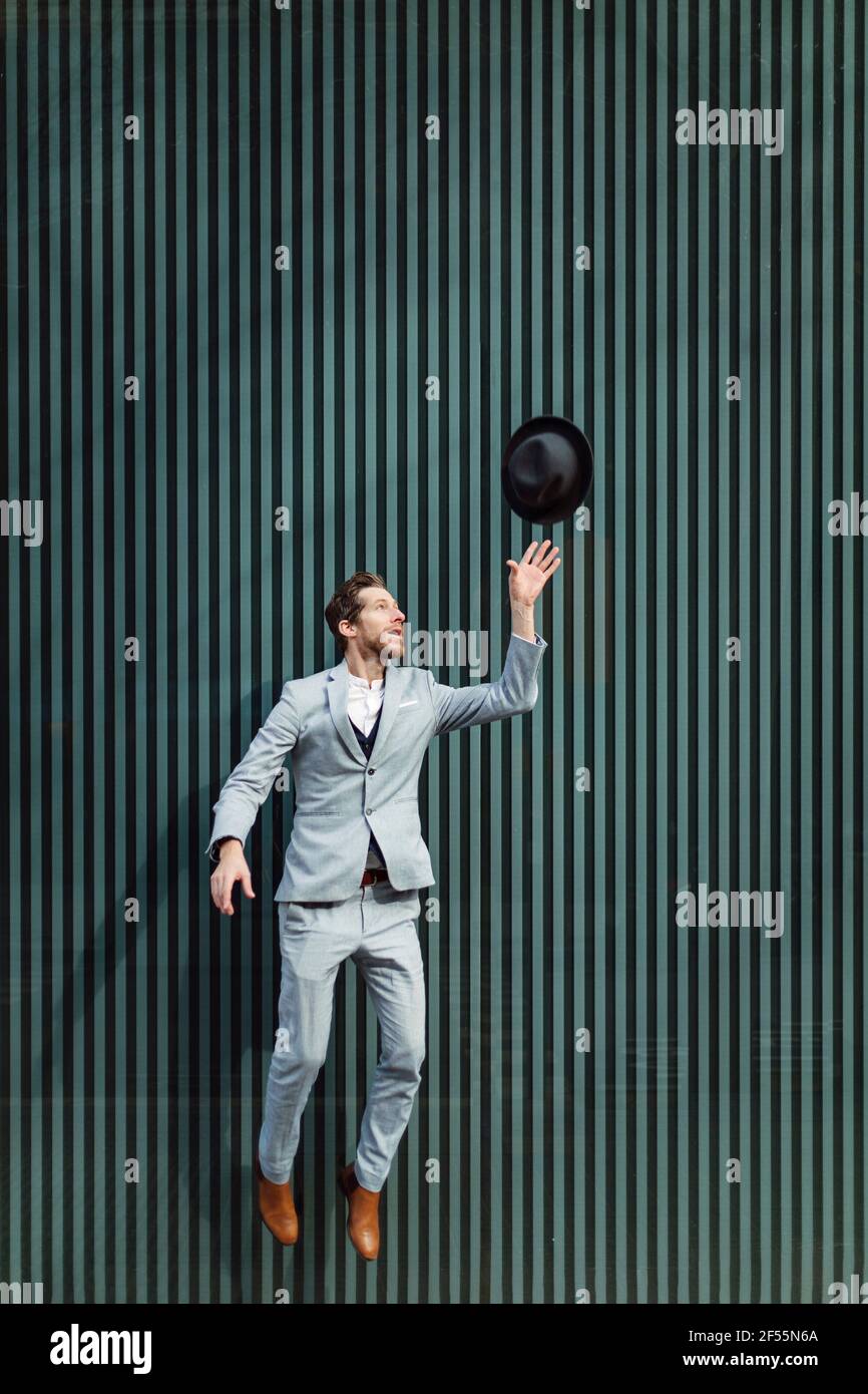 Male professional jumping while throwing hat against wall Stock Photo ...