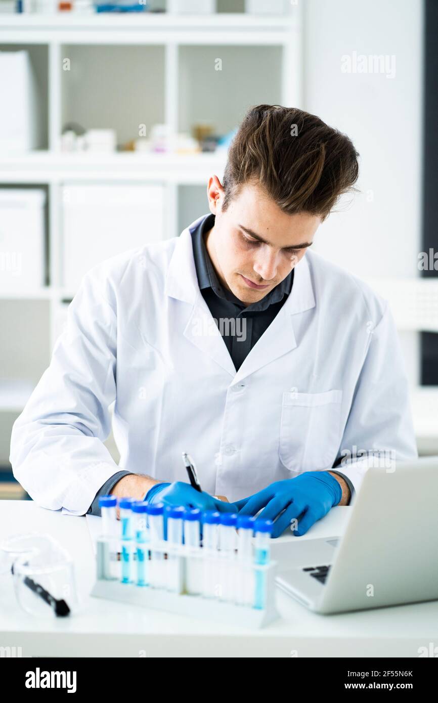 Young scientist writing notes while sitting at desk in laboratory Stock ...