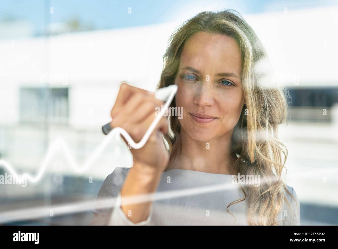 Female entrepreneur drawing on glass window while working at modern ...