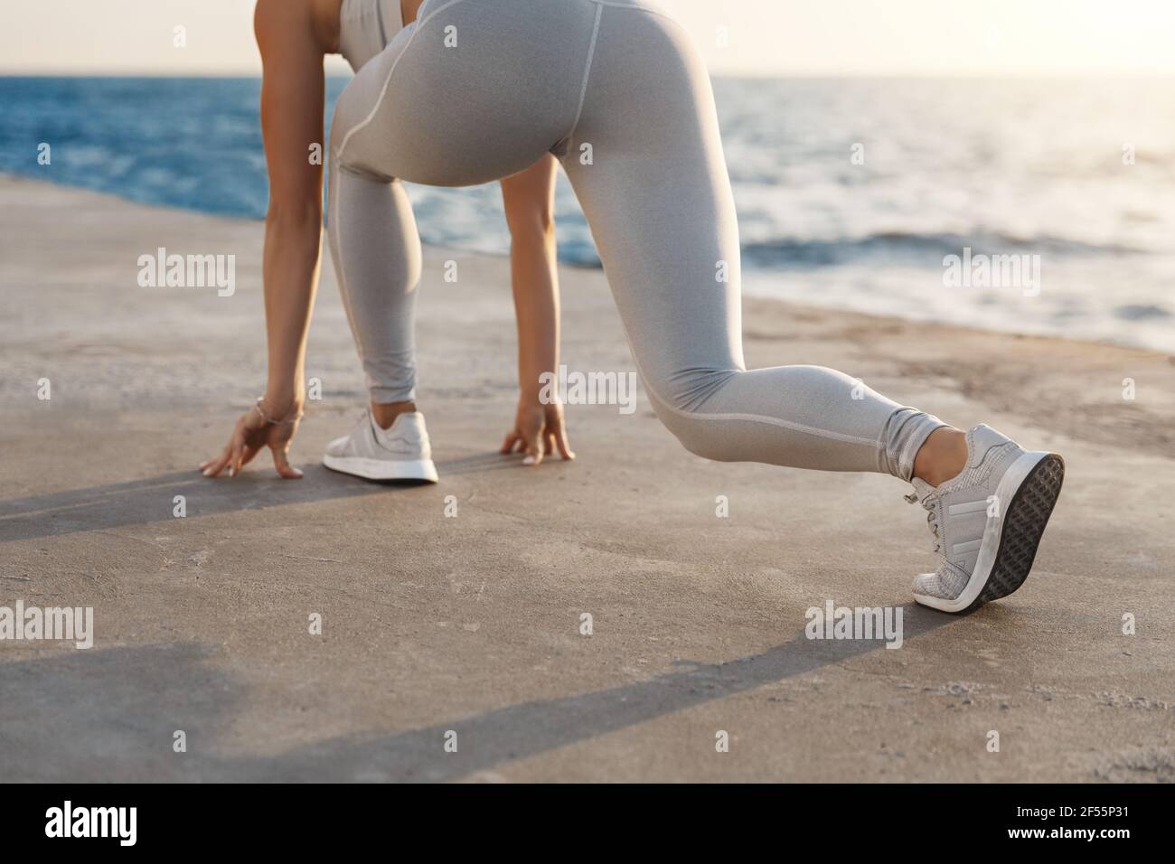 Rear-view behind woman ready race standing low-start on sea quay during ...