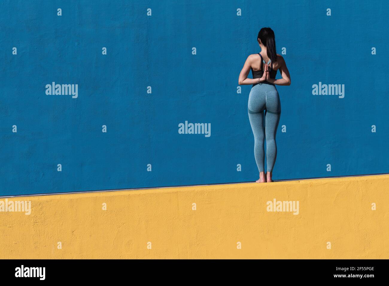 Woman with hand behind back doing hands clasped in front of wall Stock ...