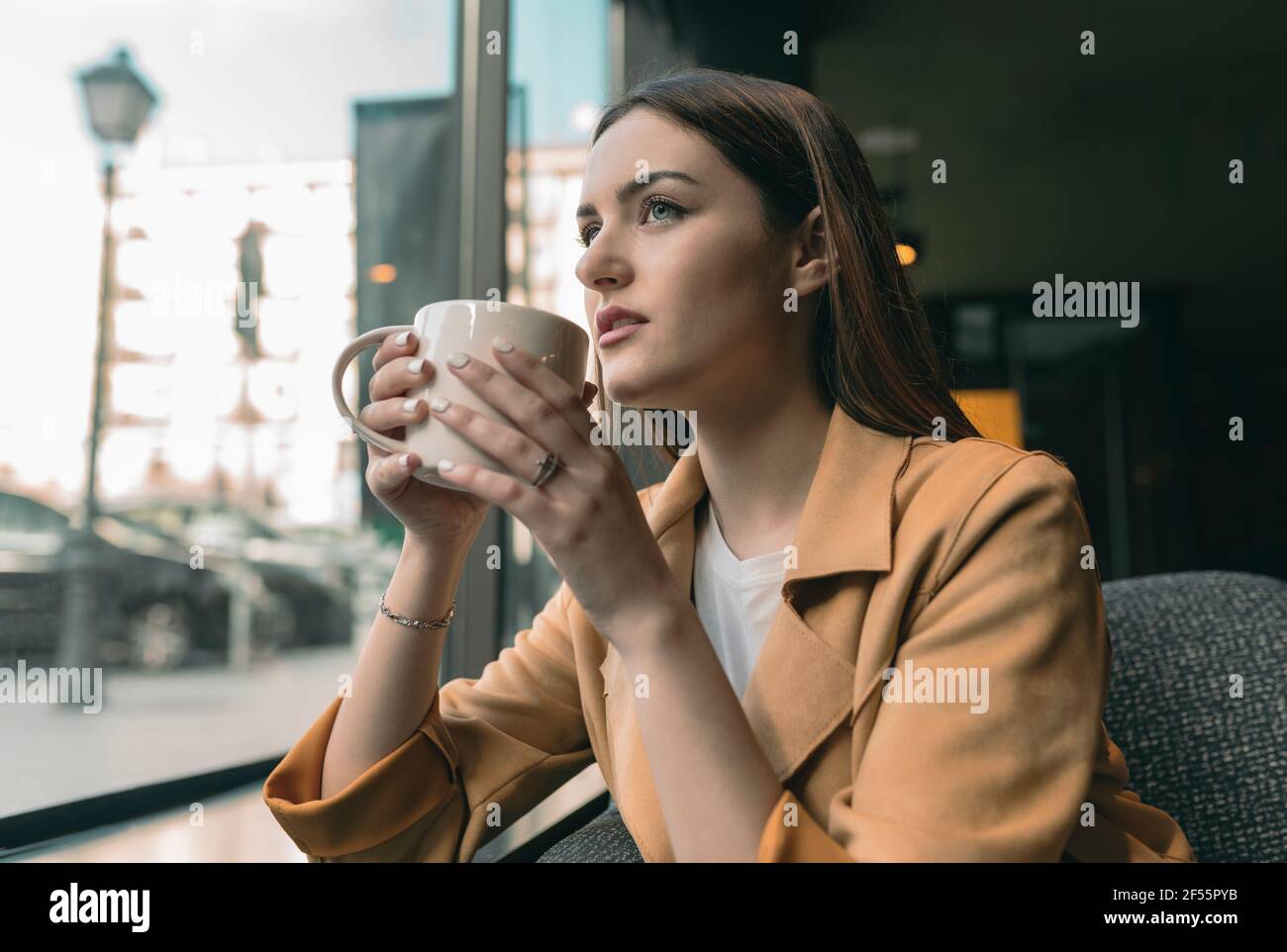 Beautiful woman drinking coffee while looking through window at cafe ...