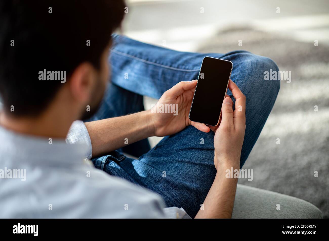 Over the shoulder view of unrecognizable man using cellphone with black empty screen for mockup ...