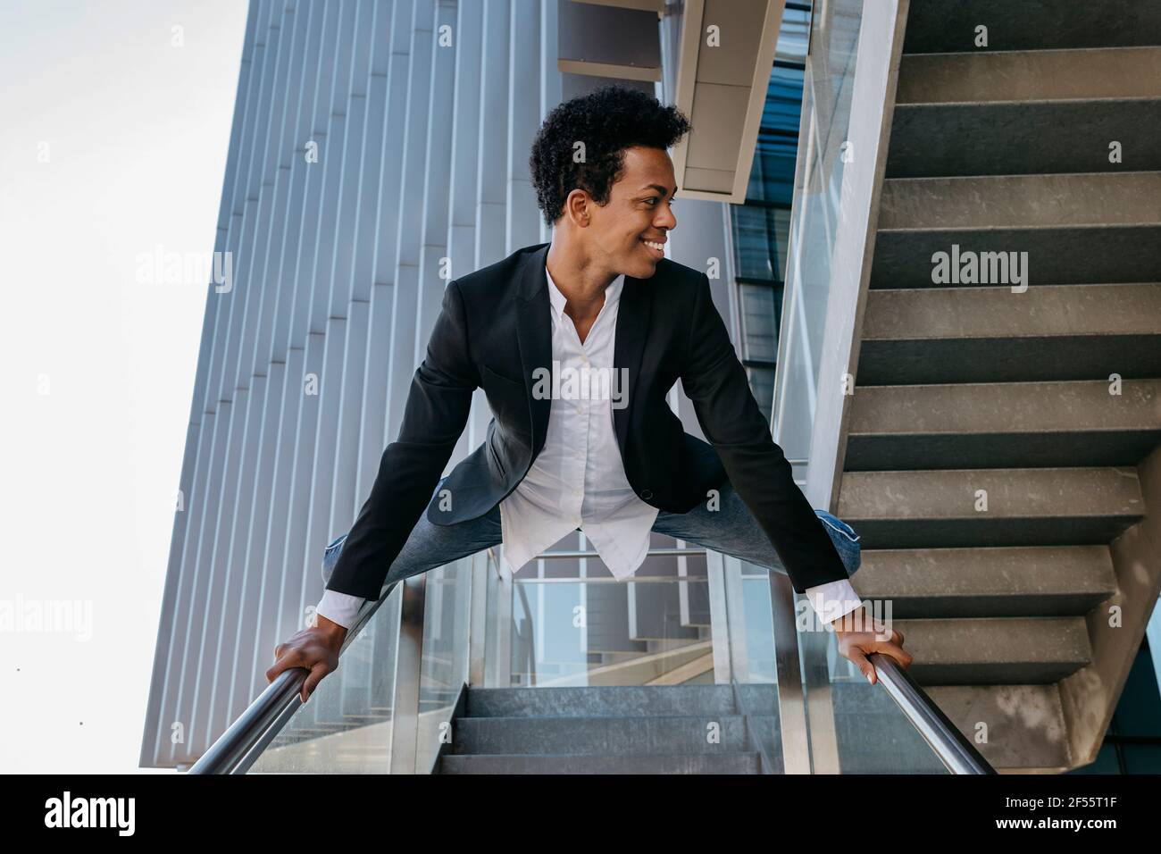 Smiling flexible businessman doing splits on staircase railing Stock ...