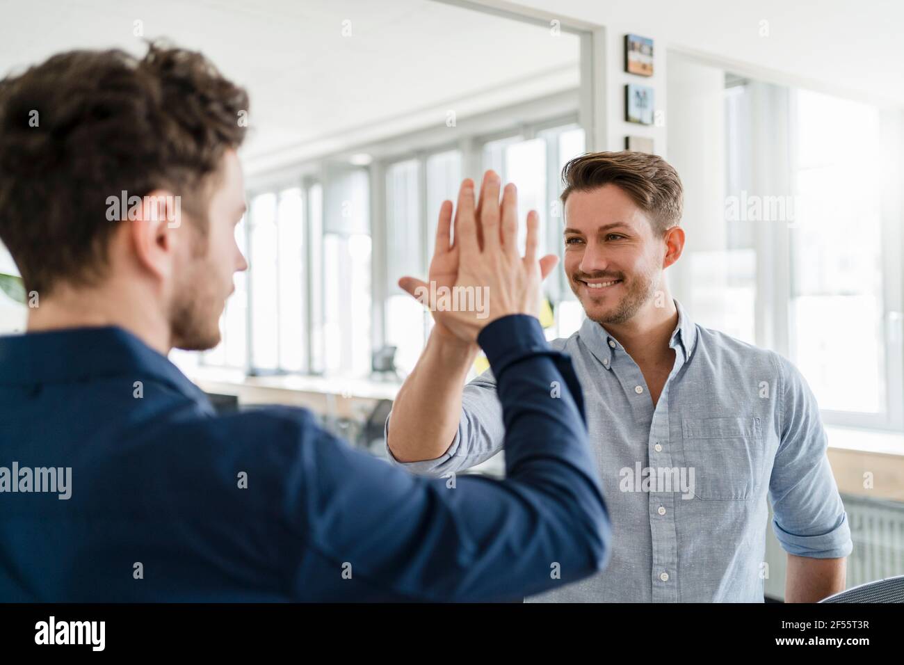 Smiling business man doing high-five with male colleague in office ...