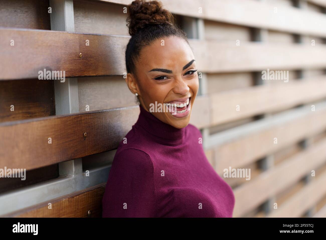 Happy woman laughing while standing against wooden wall Stock Photo - Alamy