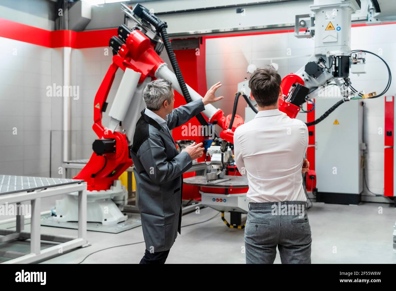 Mature engineer in jacket explaining robotics to young man in industry ...