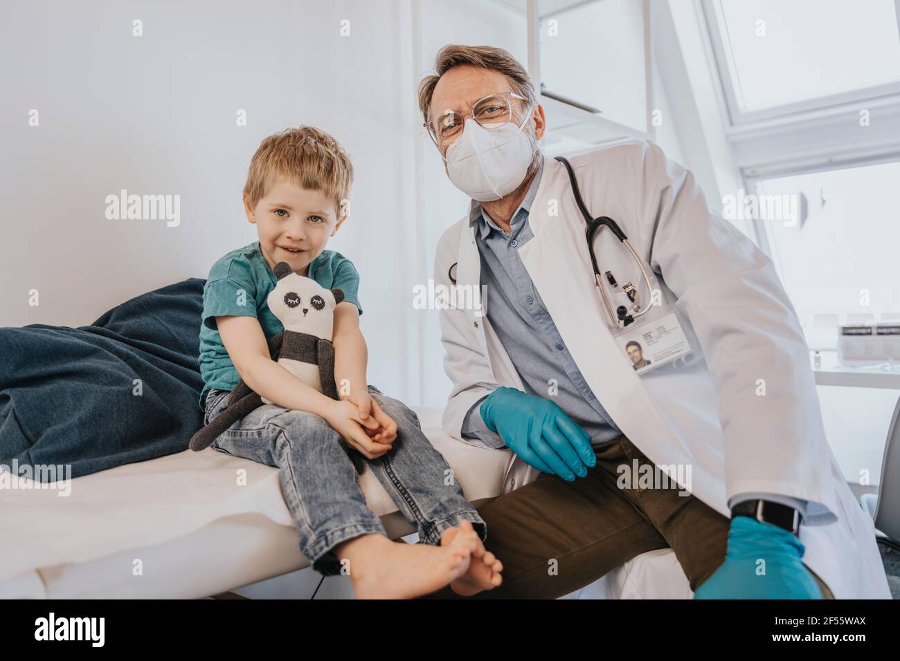 Doctor with protective face mask sitting by boy at examination room ...