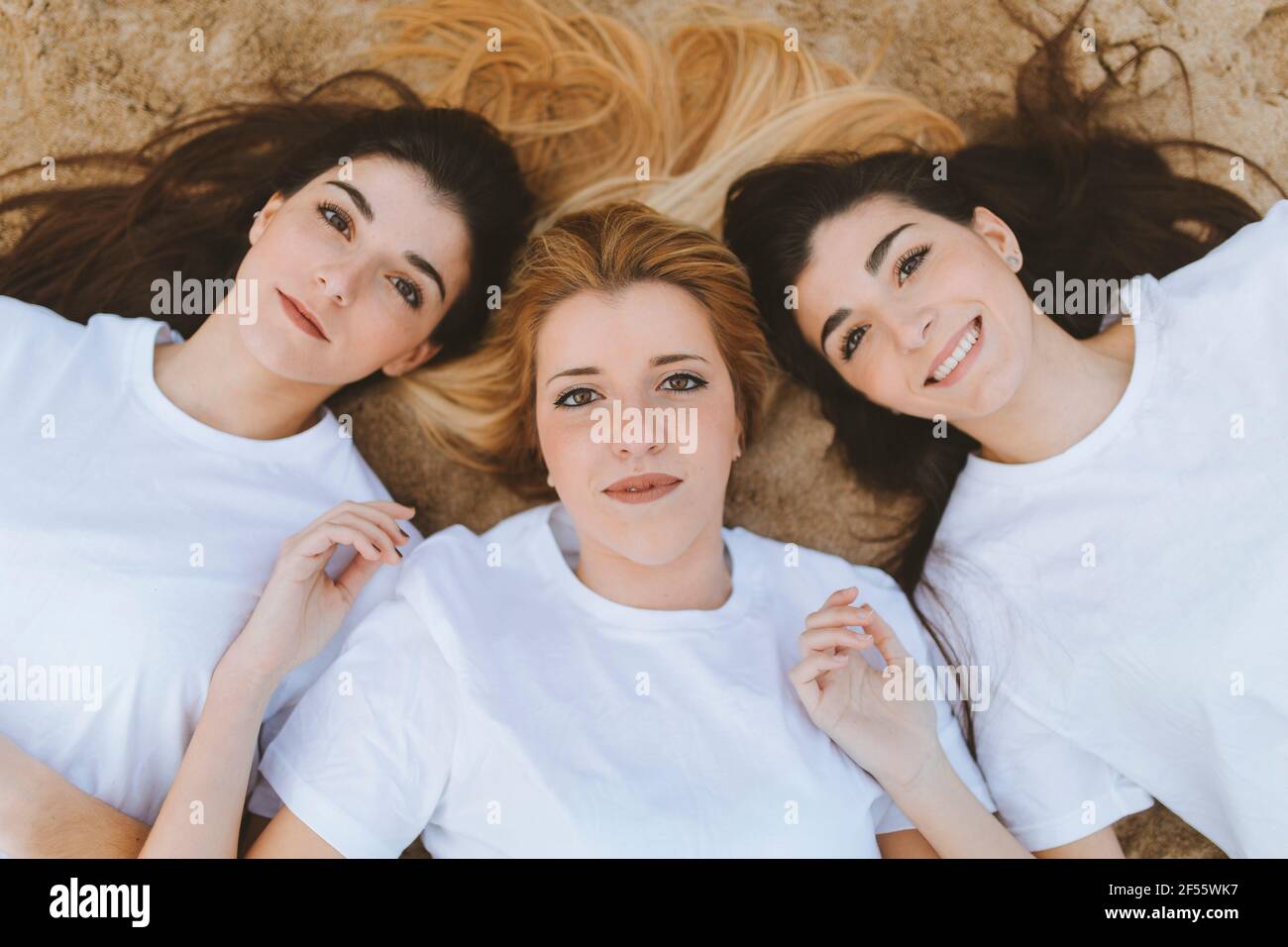Beautiful smiling female friends lying down on sand during vacations ...