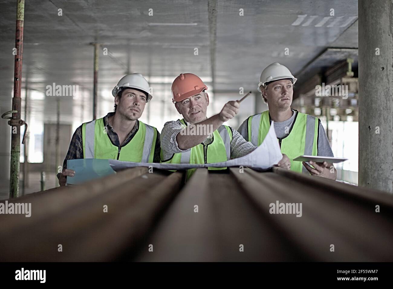 Male construction worker discussing plan with coworkers at construction ...