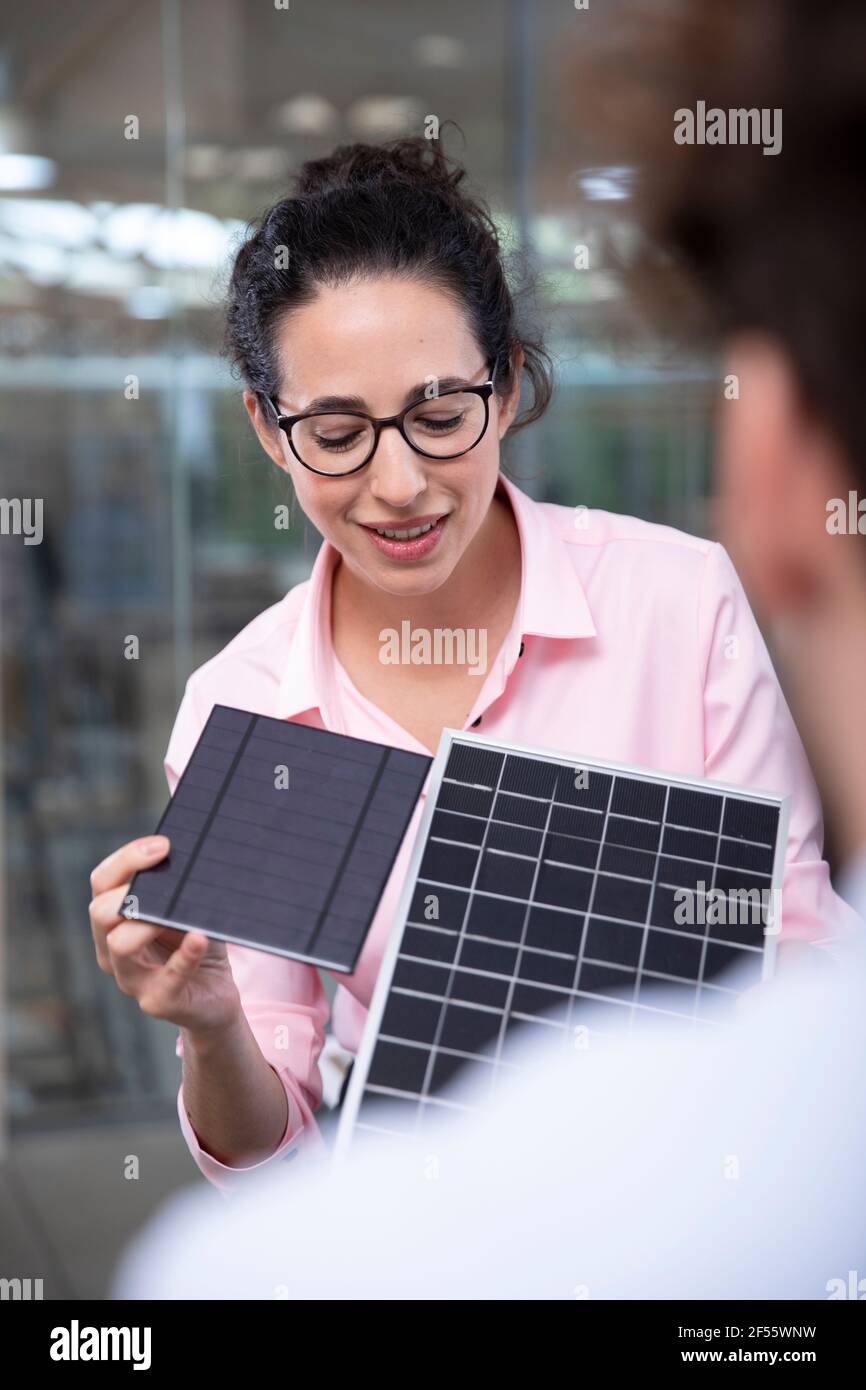 Female entrepreneur showing solar panel model to colleague in office ...