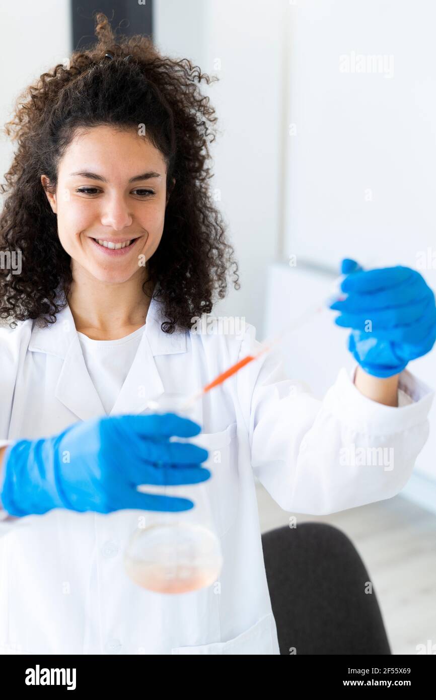 Smiling female doctor mixing solution in beaker through pipette at ...