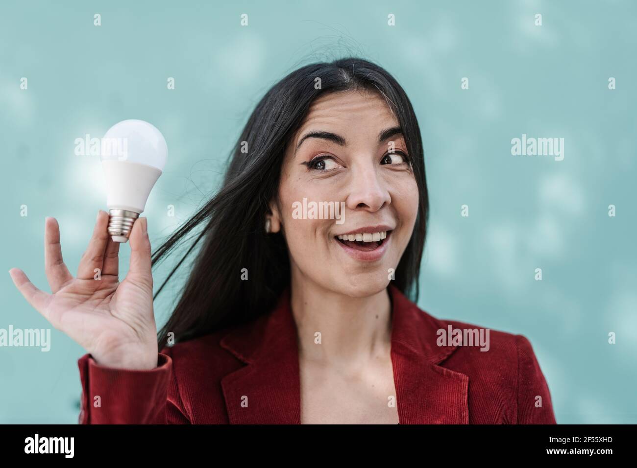 Surprised businesswoman holding light bulb against turquoise wall Stock ...