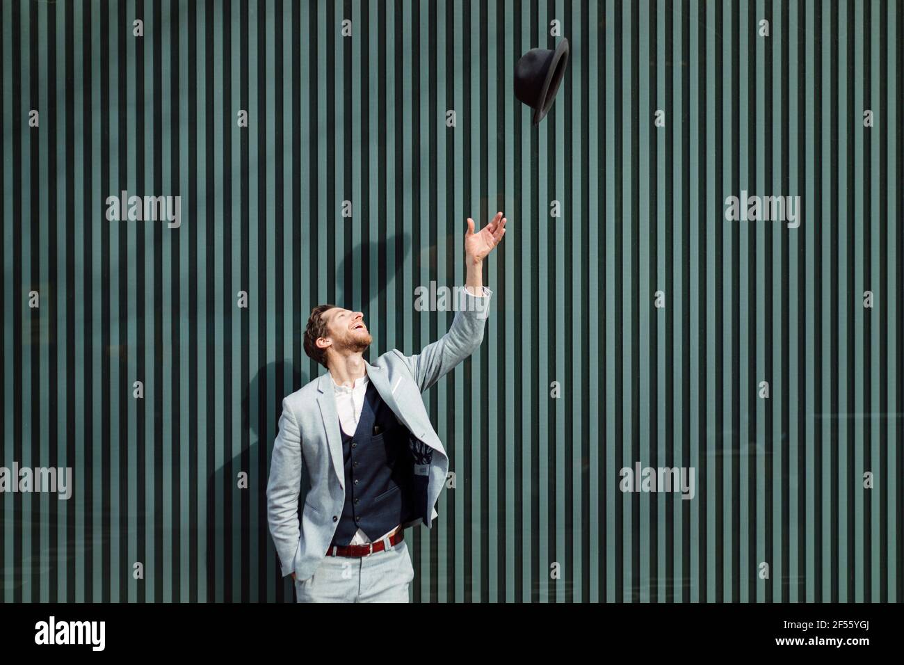 Happy male entrepreneur throwing hat while standing against wall Stock ...