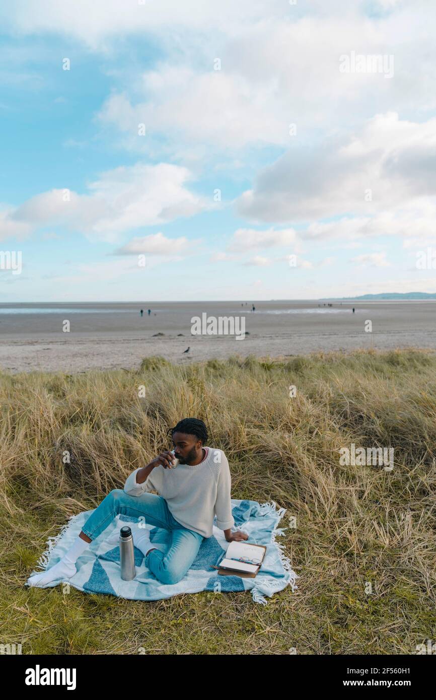 Man drinking tea while sitting amidst dried plants at beach Stock Photo ...