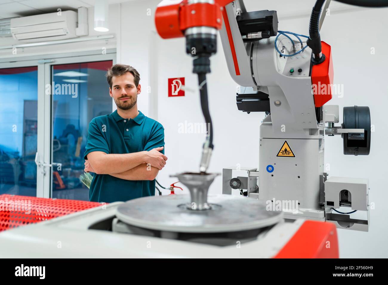 Smiling young man with arms crossed standing at automatic machinery in ...