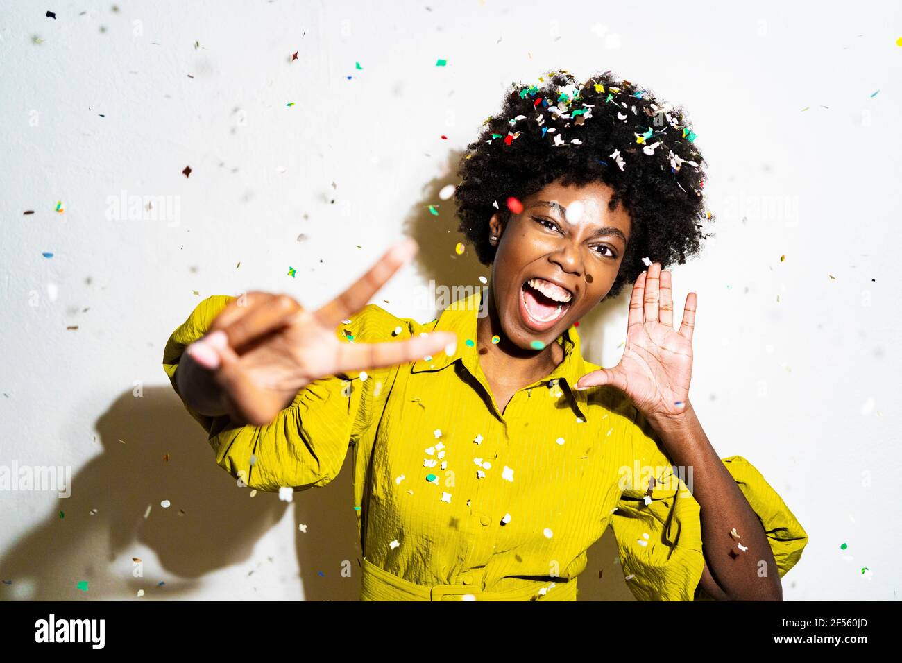 Confetti falling on woman gesturing peace sign while standing white ...