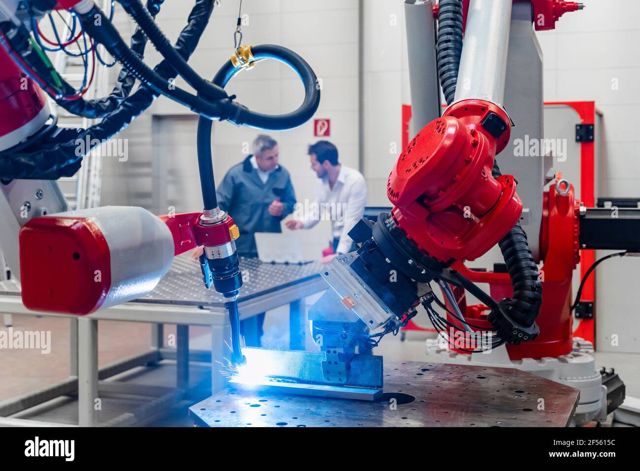 Robotic arm welding while male engineers discussing in factory Stock ...
