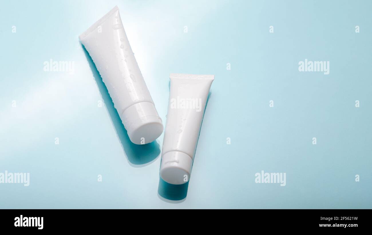 White cosmetic product in tubes on color background with water drops ...