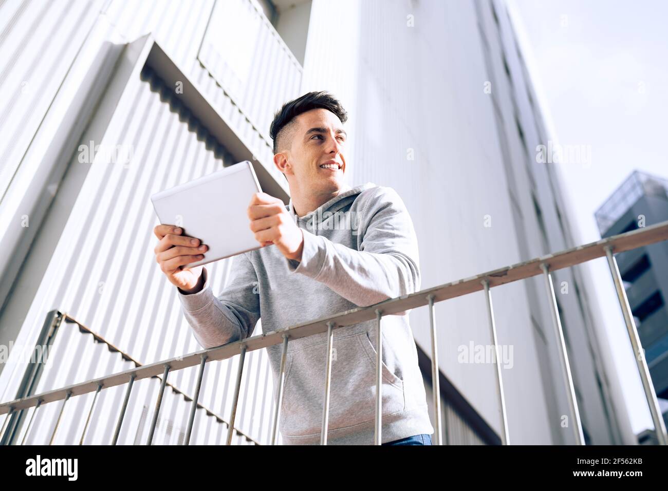 Handsome man looking away while holding digital tablet leaning on ...