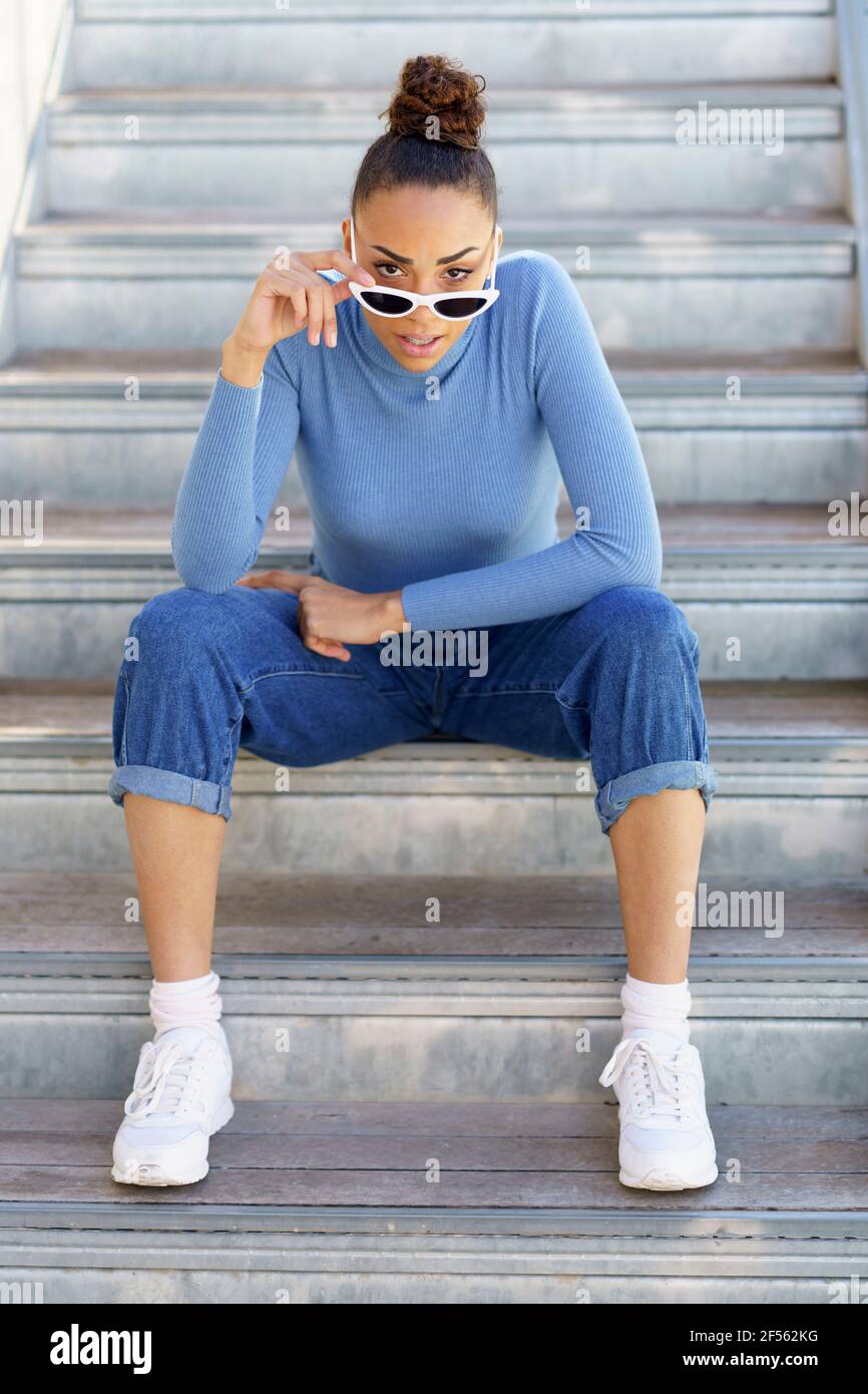 Woman with sunglasses staring while sitting on steps Stock Photo - Alamy
