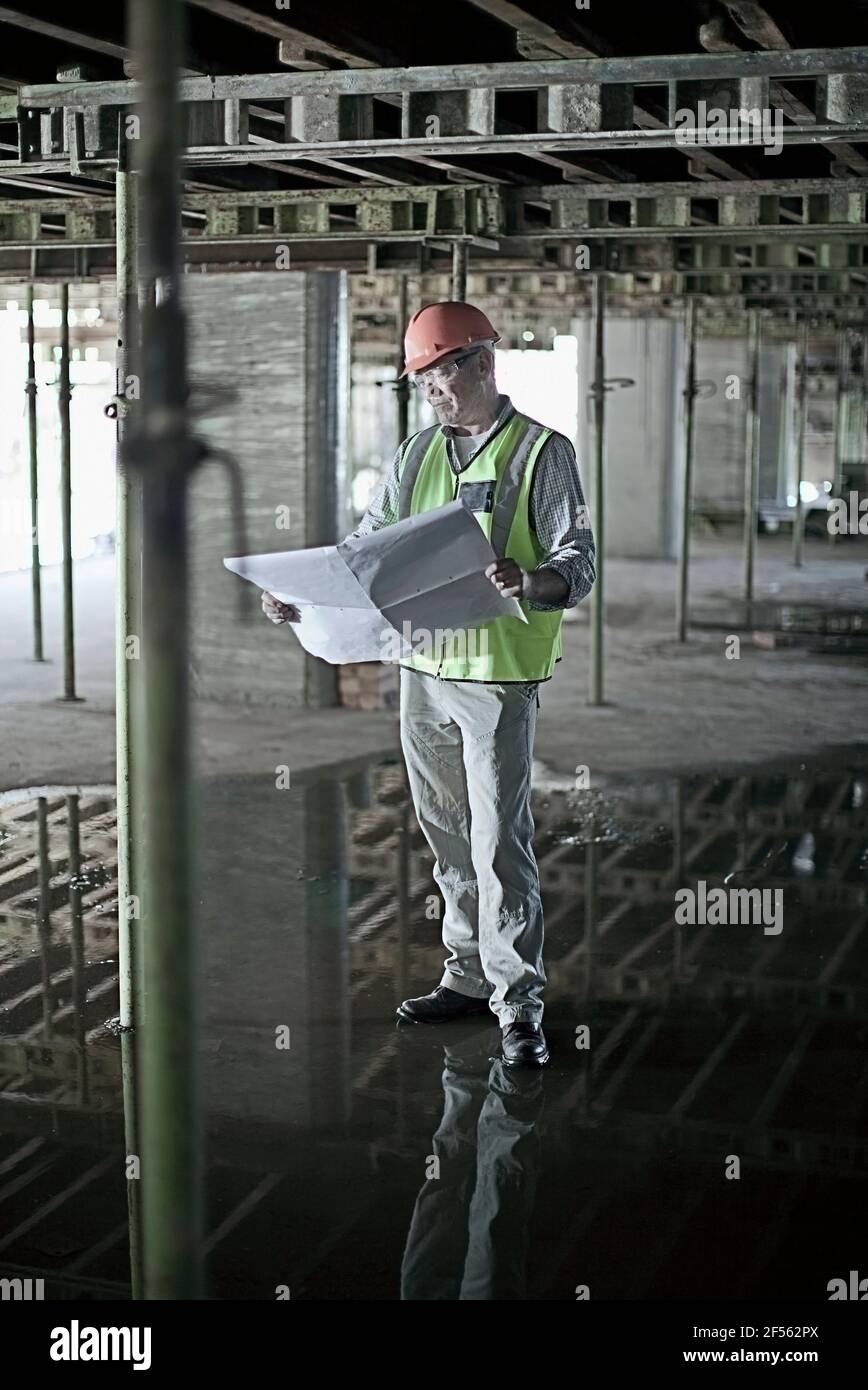 Construction worker standing at construction site with plans in hands ...