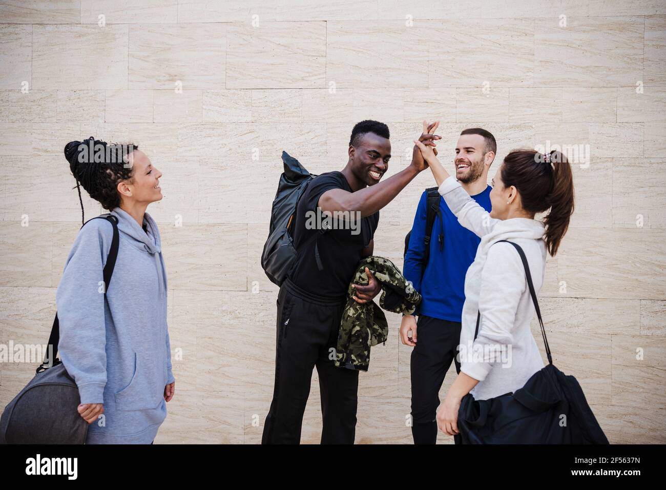 Happy male and female athlete giving high-five while standing by wall ...