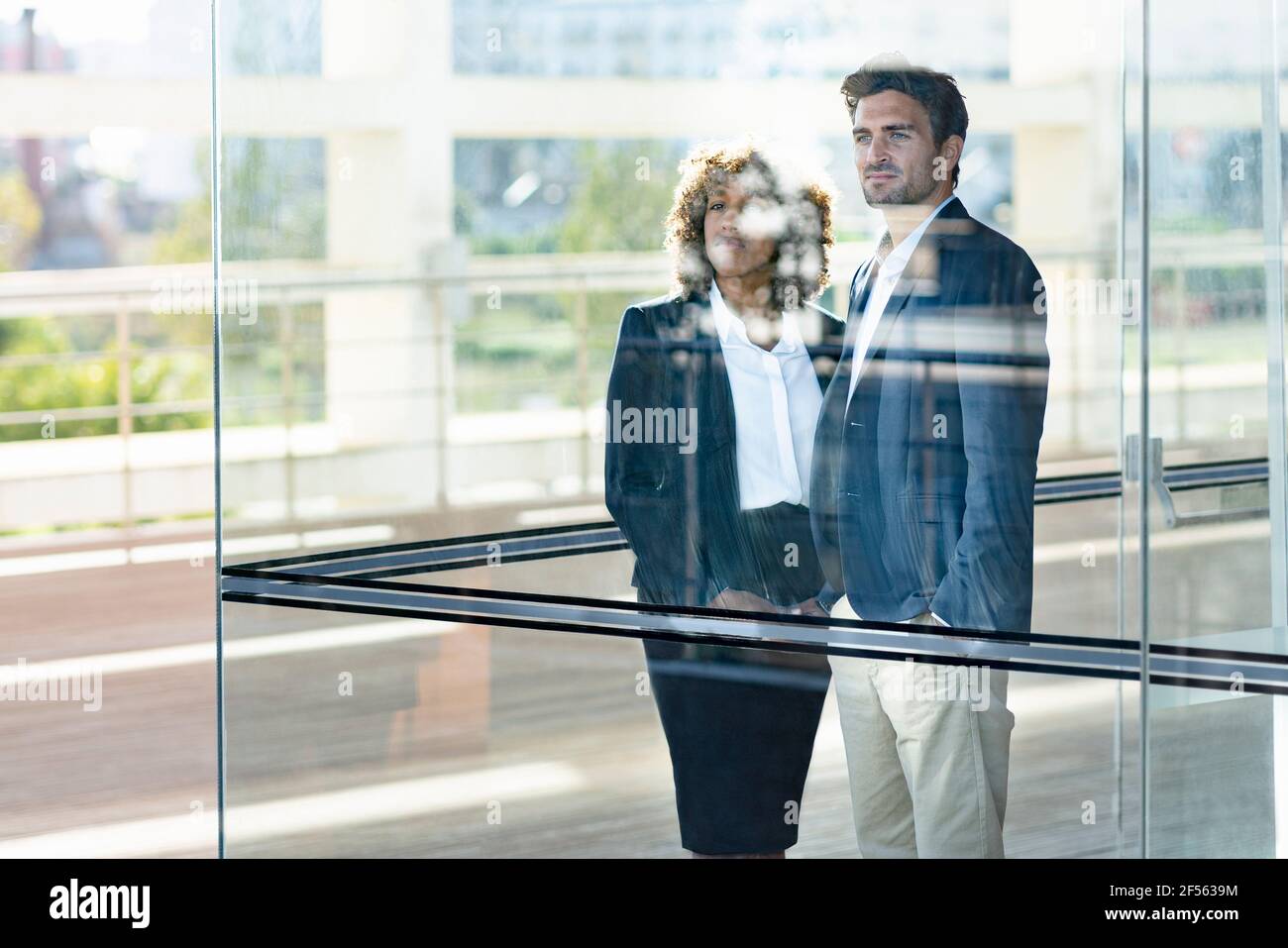Business people looking away while standing by glass window in modern ...
