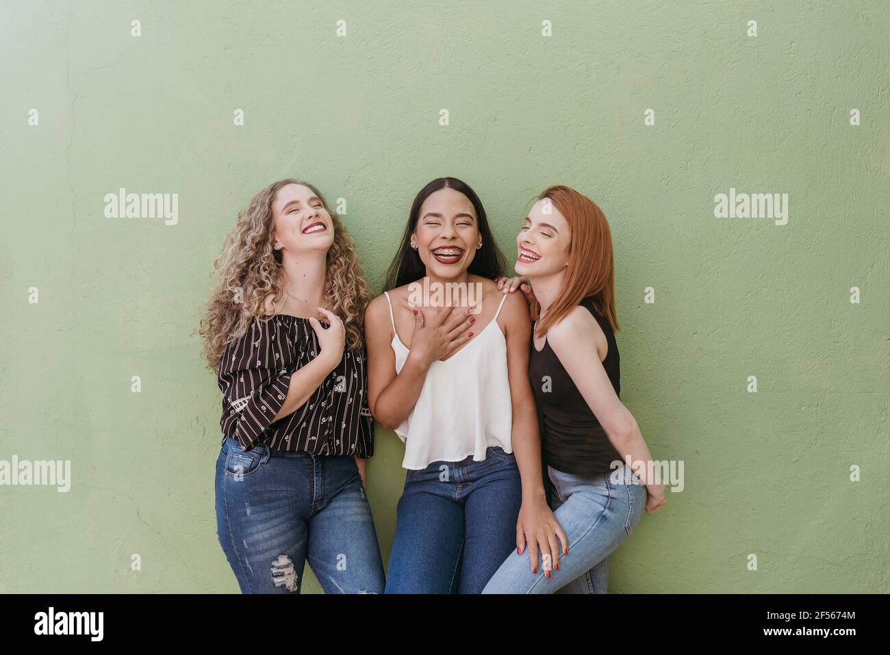 Carefree young women laughing while standing against green wall Stock ...