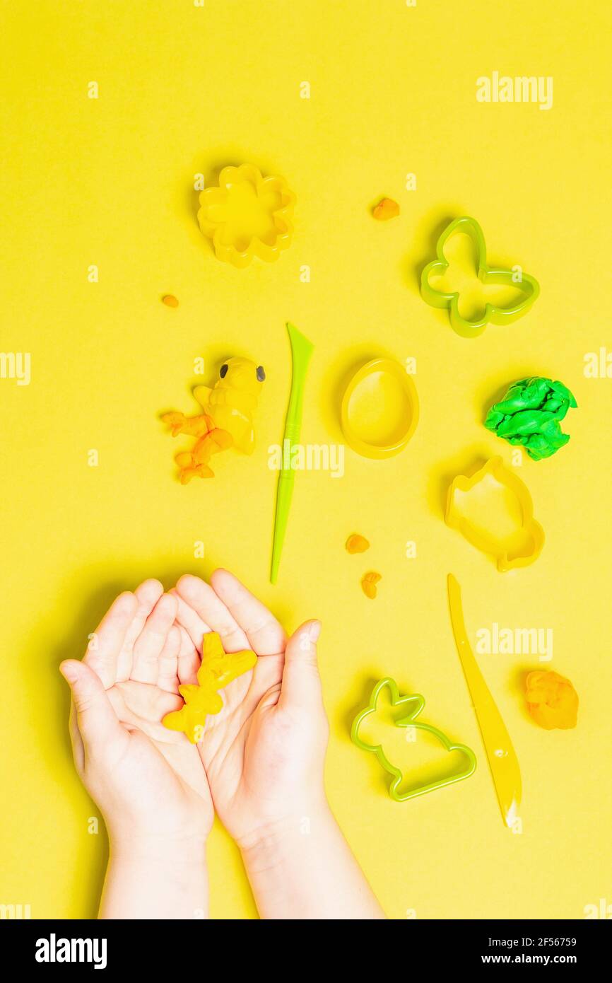 Children hands playing with colorful modeling clay on yellow background ...