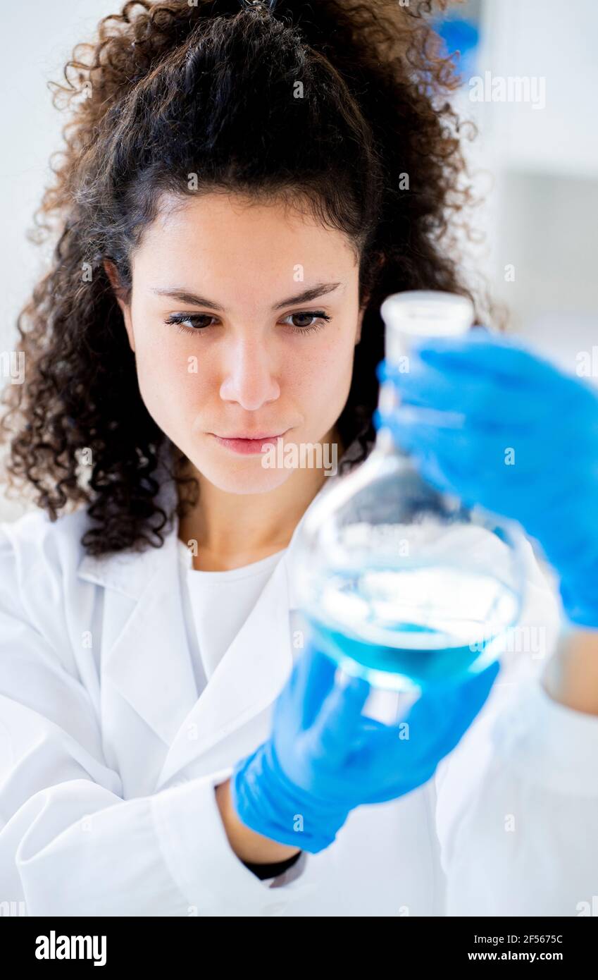 Female researcher examining beaker with chemical solution in hospital ...