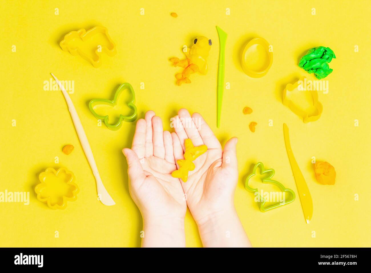 Children hands playing with colorful modeling clay on yellow background ...