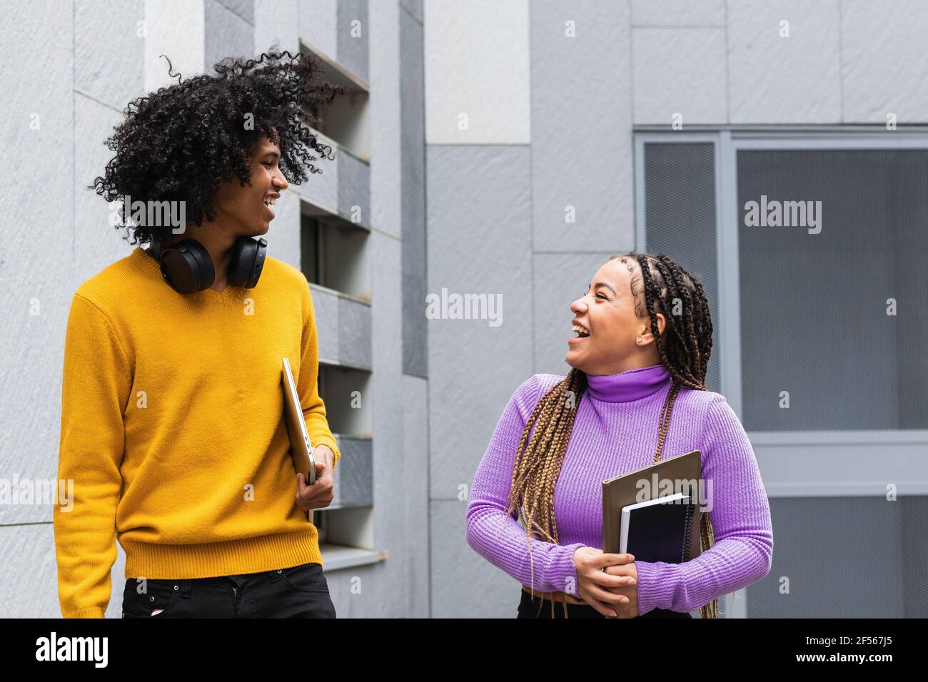 Smiling students looking at each other while standing at university ...