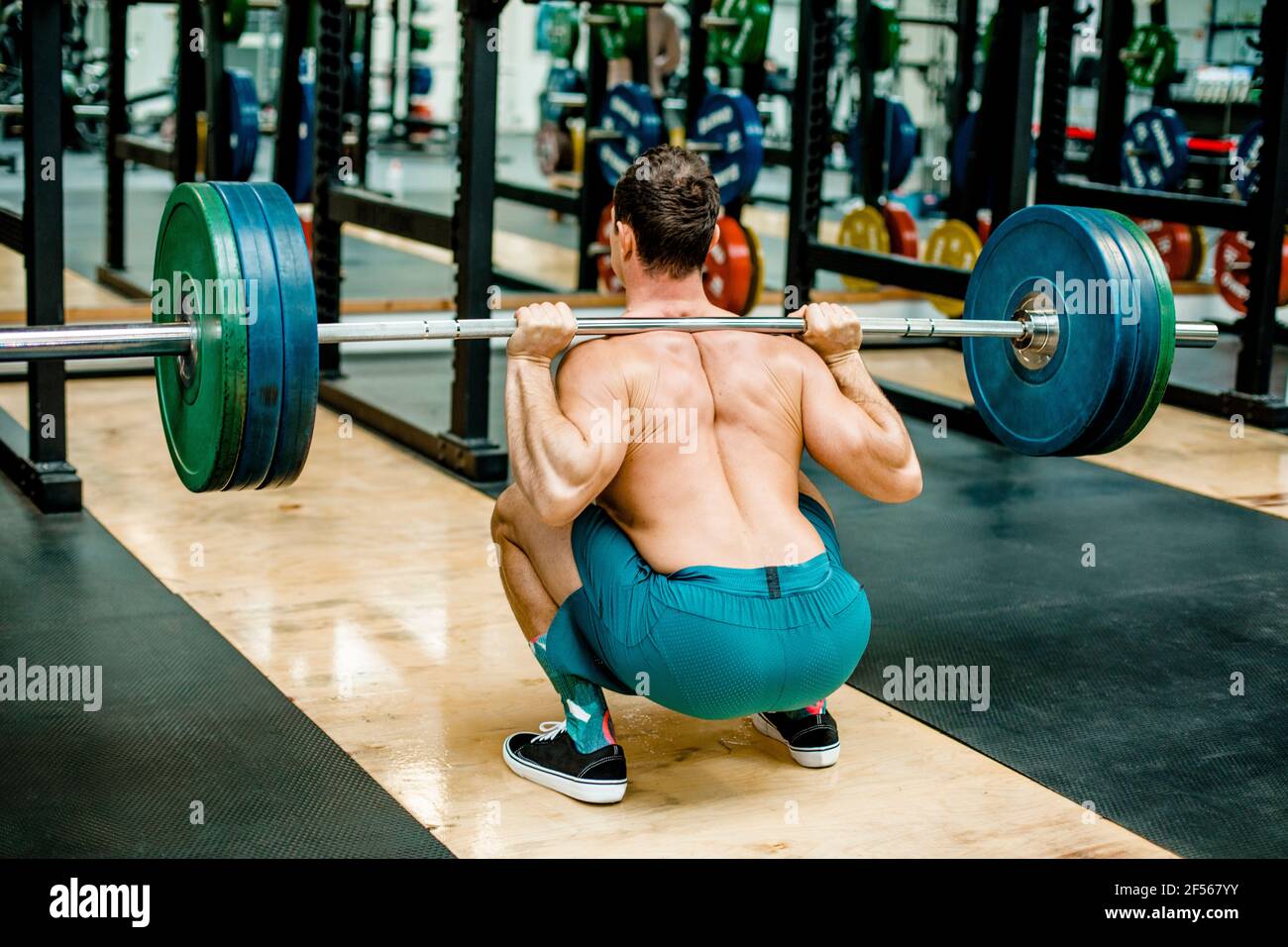 Man in squatting position weightlifting at gym Stock Photo - Alamy