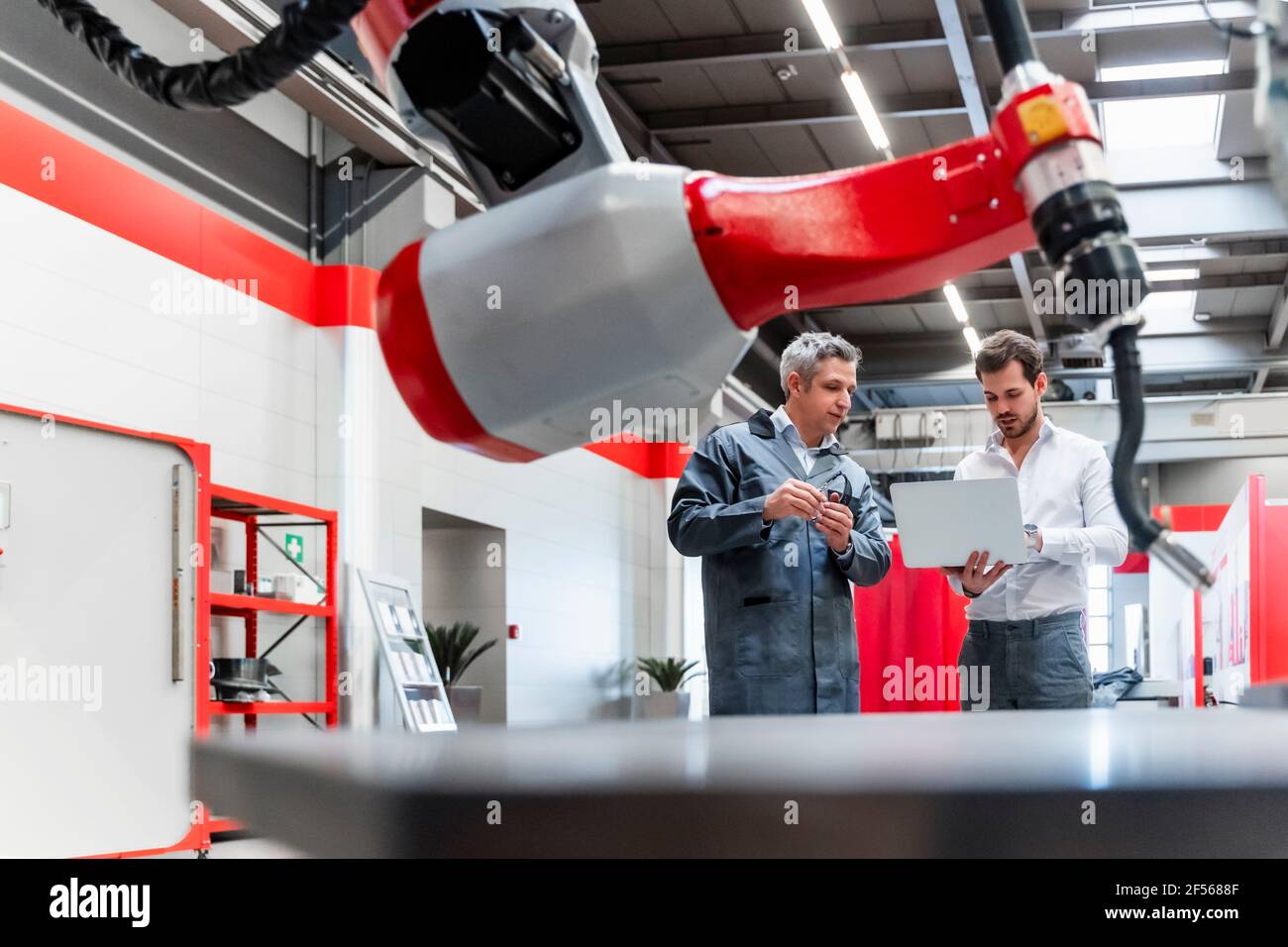 Male entrepreneurs with laptop seen through robotics in factory Stock ...