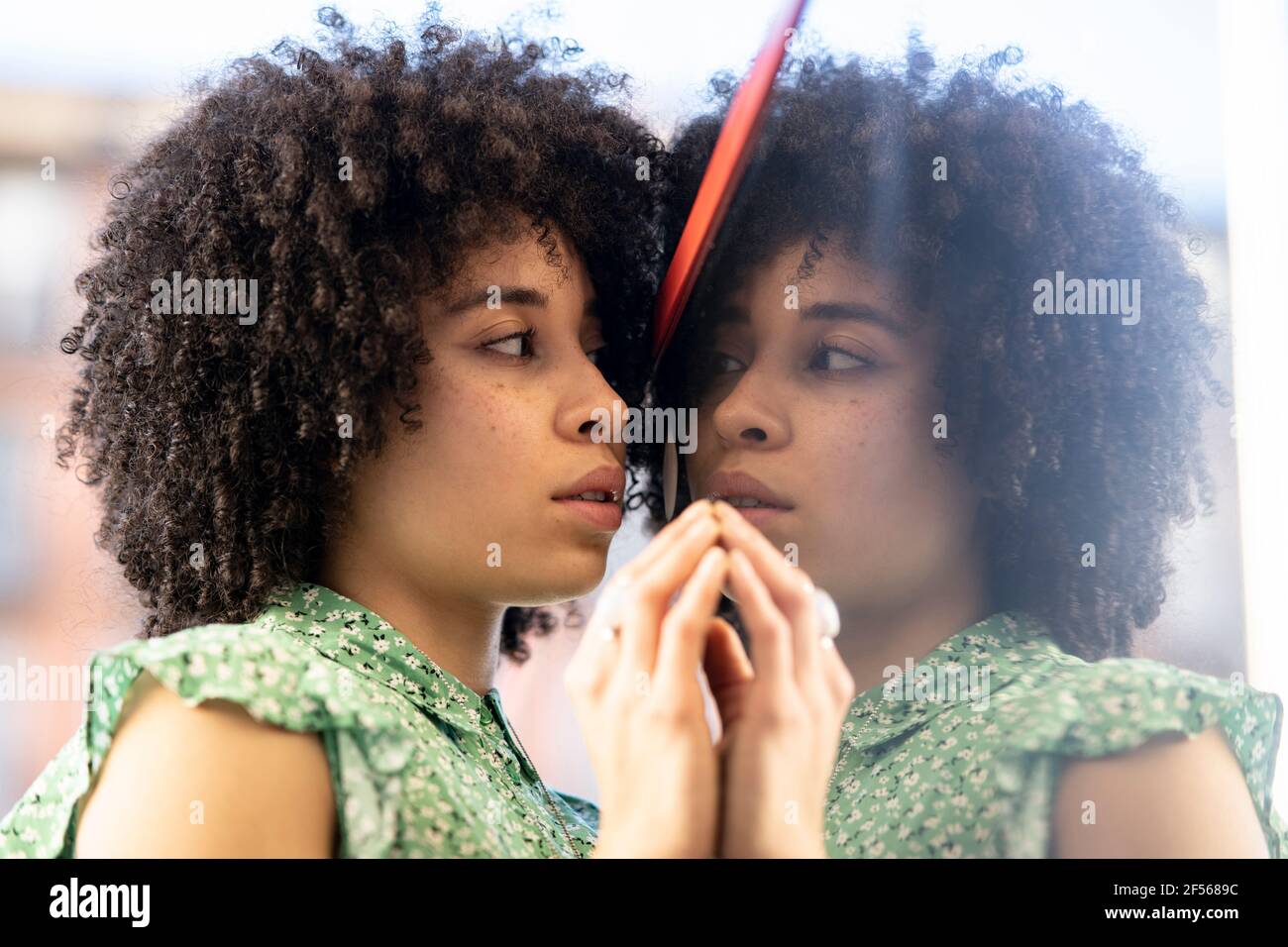 Young afro woman looking at reflection in glass wall Stock Photo - Alamy