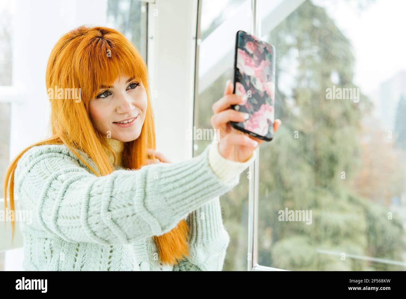 Smiling beautiful woman taking selfie by window Stock Photo - Alamy