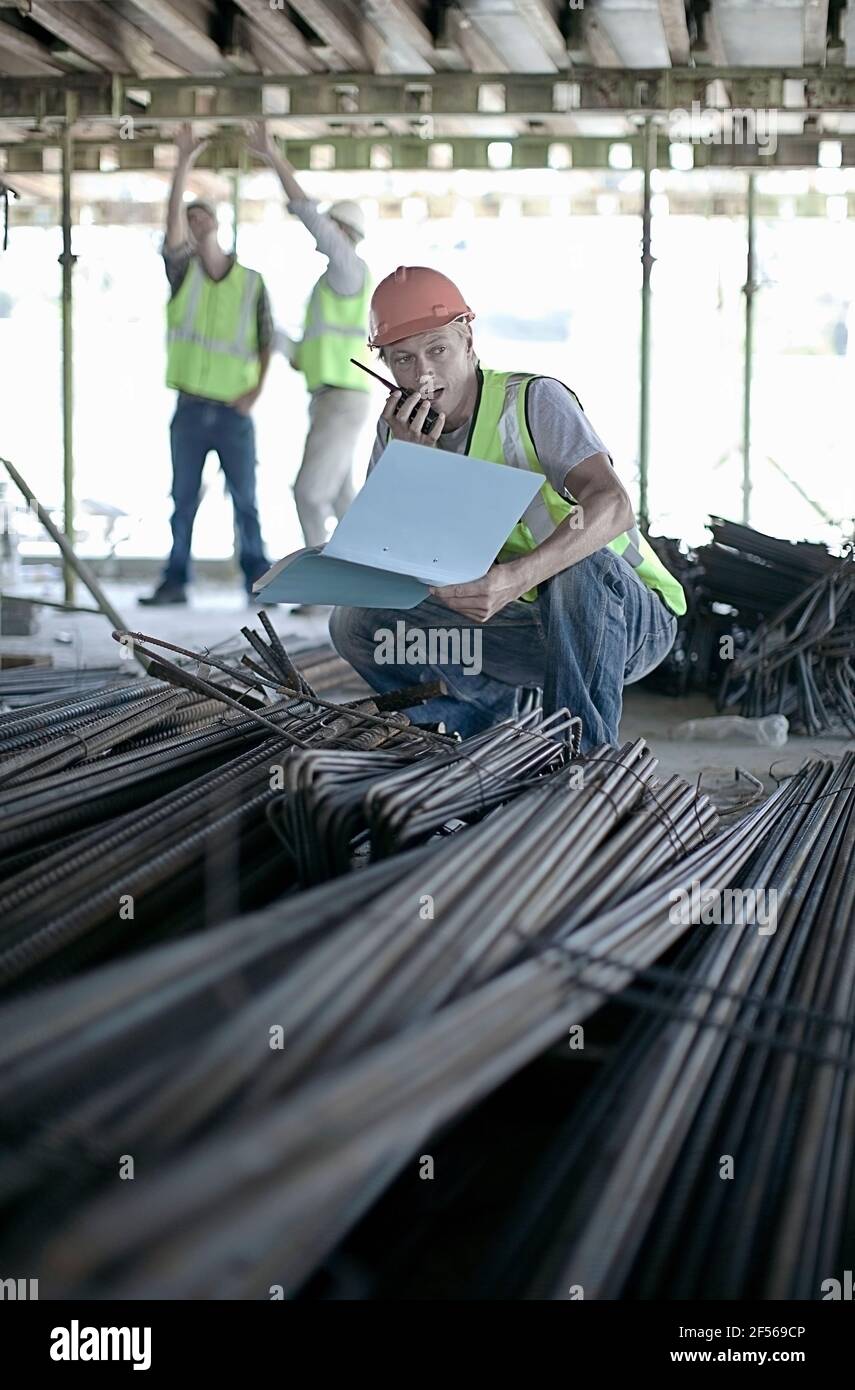 Male construction worker talking on walkie-talkie while coworkers ...