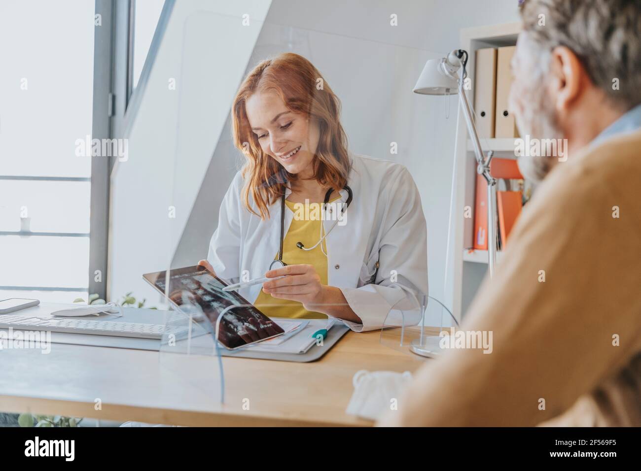 Smiling doctor explaining patient over x-ray while sitting by screen ...