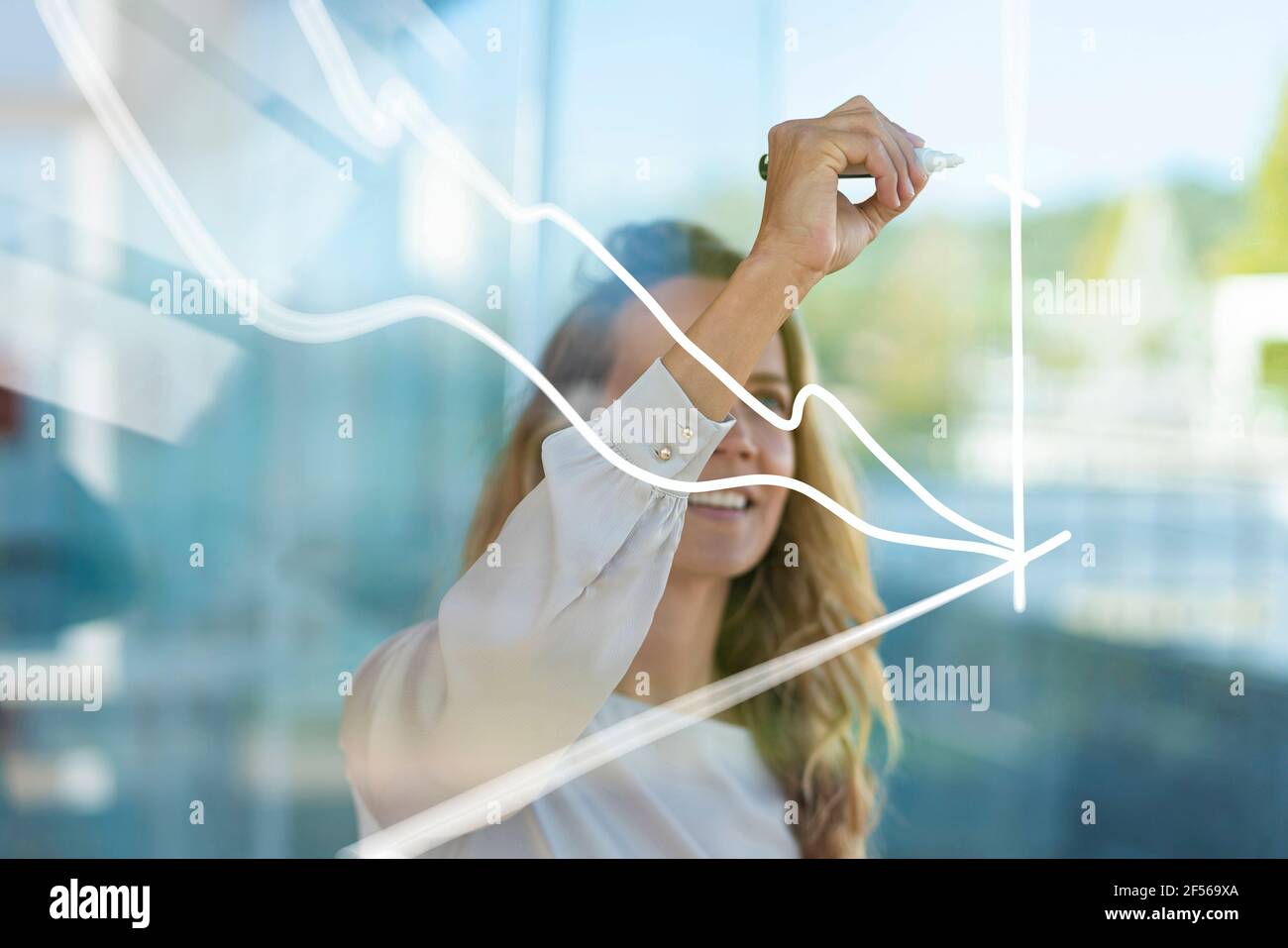 Businesswoman drawing graph on glass while standing at modern office ...