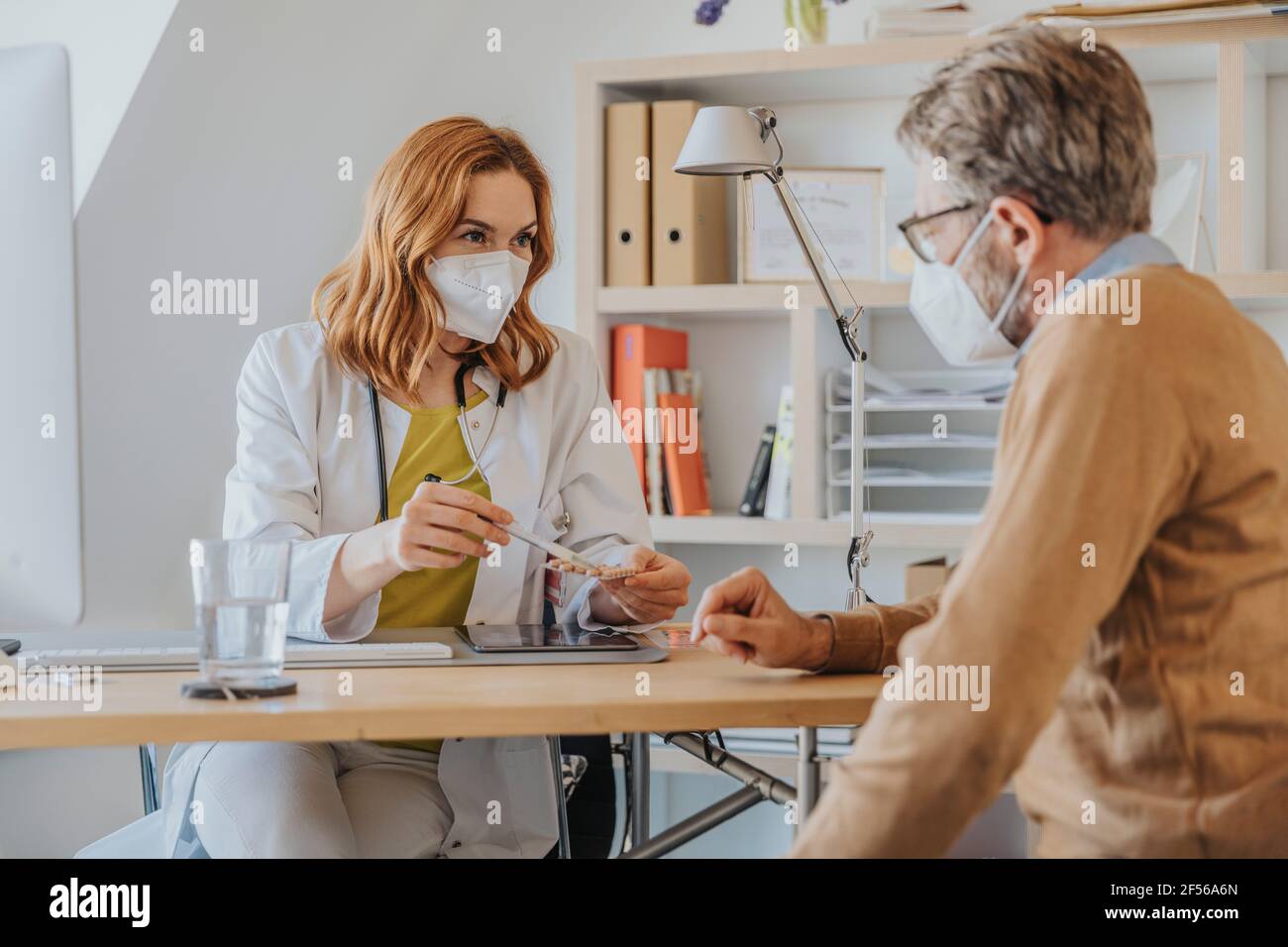 Doctor with protective face mask explaining over medication at doctor's ...